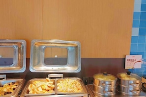 Buffet com diversos alimentos em recipientes metálicos.