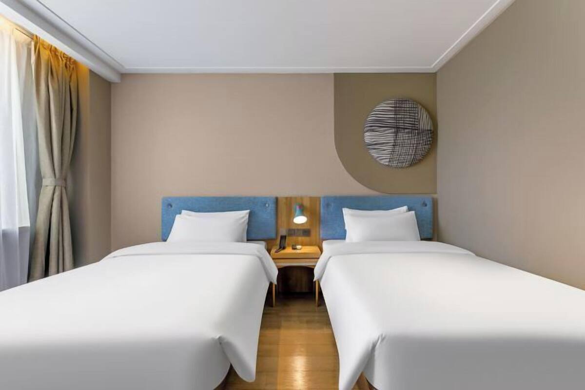 Quarto de hotel com duas camas, um adorno redondo na parede, uma mesa de cabeceira e uma luminária.
