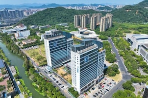 Um edifício alto com design moderno, rodeado por vegetação e outros edifícios.