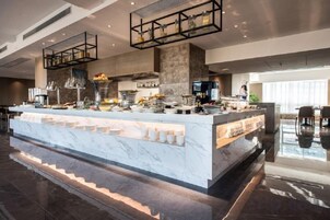 Uma área de bar moderna com bancada de mármore, iluminação pendente e um espaço de estar com cadeiras.