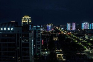 Paisagem urbana noturna com edifícios iluminados e uma rua movimentada.