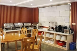 Espaço de café da manhã com mesa e cadeiras de madeira, buffet com distribuidores de alimentos e um canto para café.
