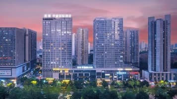 Paisagem urbana com edifícios altos, um deles com letreiros iluminados e outro com entrada destacada.