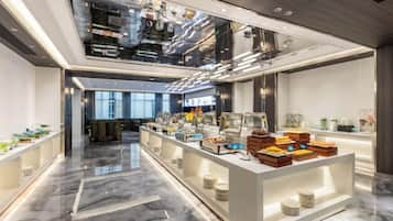 Um hall de hotel moderno com uma recepção central, um bar de café de vidro e um chão de mármore polido.