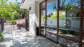 Uma varanda com porta de vidro, grades de metal e vista para uma rua arborizada com carros estacionados.