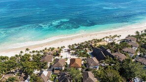 Vista aérea de um resort à beira-mar com chalés de telhado de palha, palmeiras e uma praia de areia.