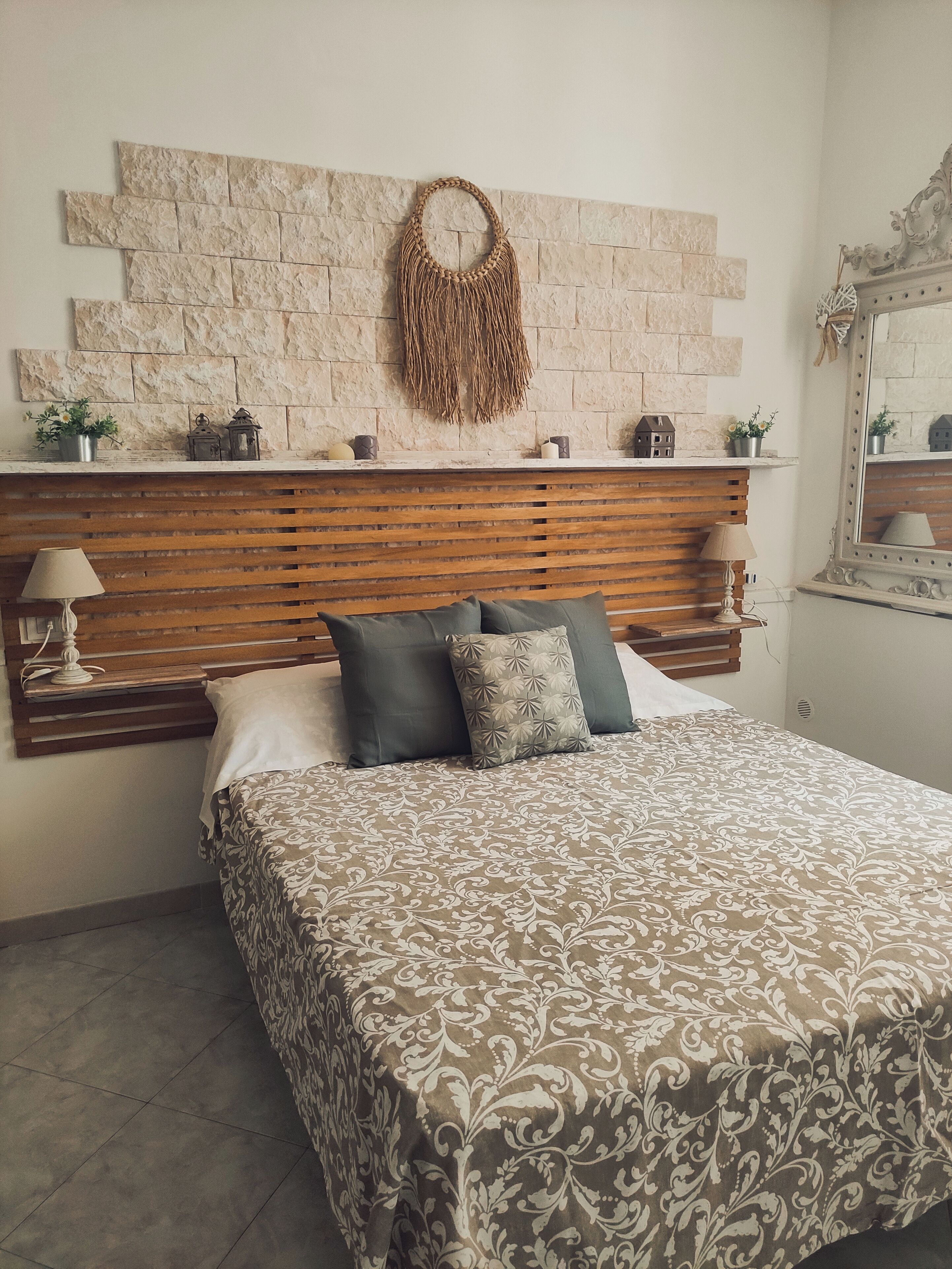 Quarto com parede de pedra, cabeceira de madeira e colcha estampada.