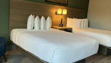 Uma cama de casal com roupa de cama branca, uma mesa de cabeceira com abajur e um quadro acima da cama.