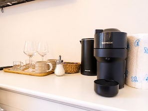 Uma cozinha compacta com cafeteira, xícaras, copos e uma cesta.