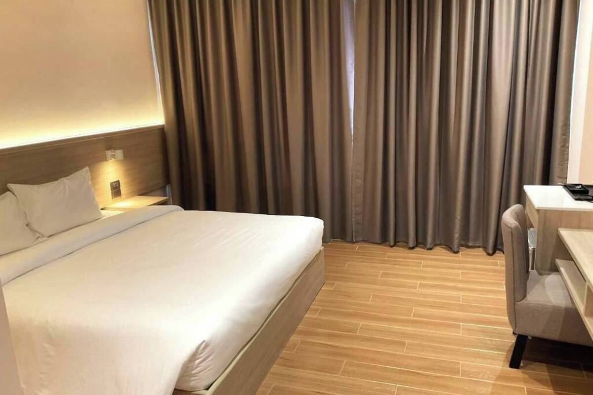 Quarto de hotel com uma cama, escrivaninha e cortinas.