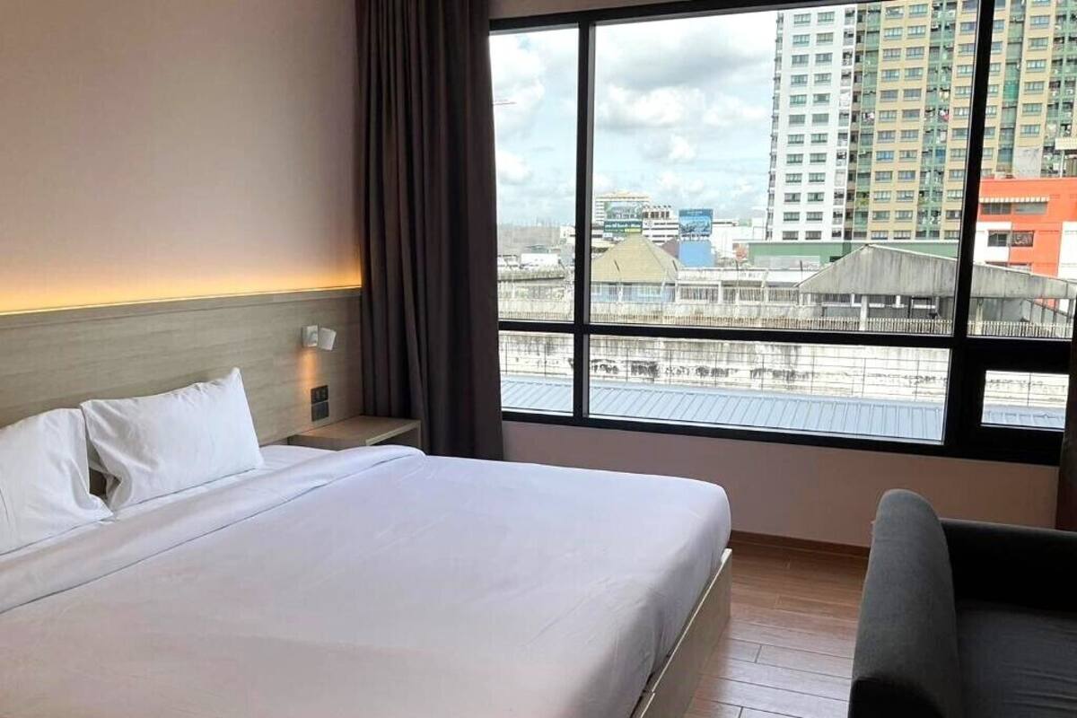 Quarto de hotel com cama grande, mesa de cabeceira, cadeira e janela com vista para a cidade.