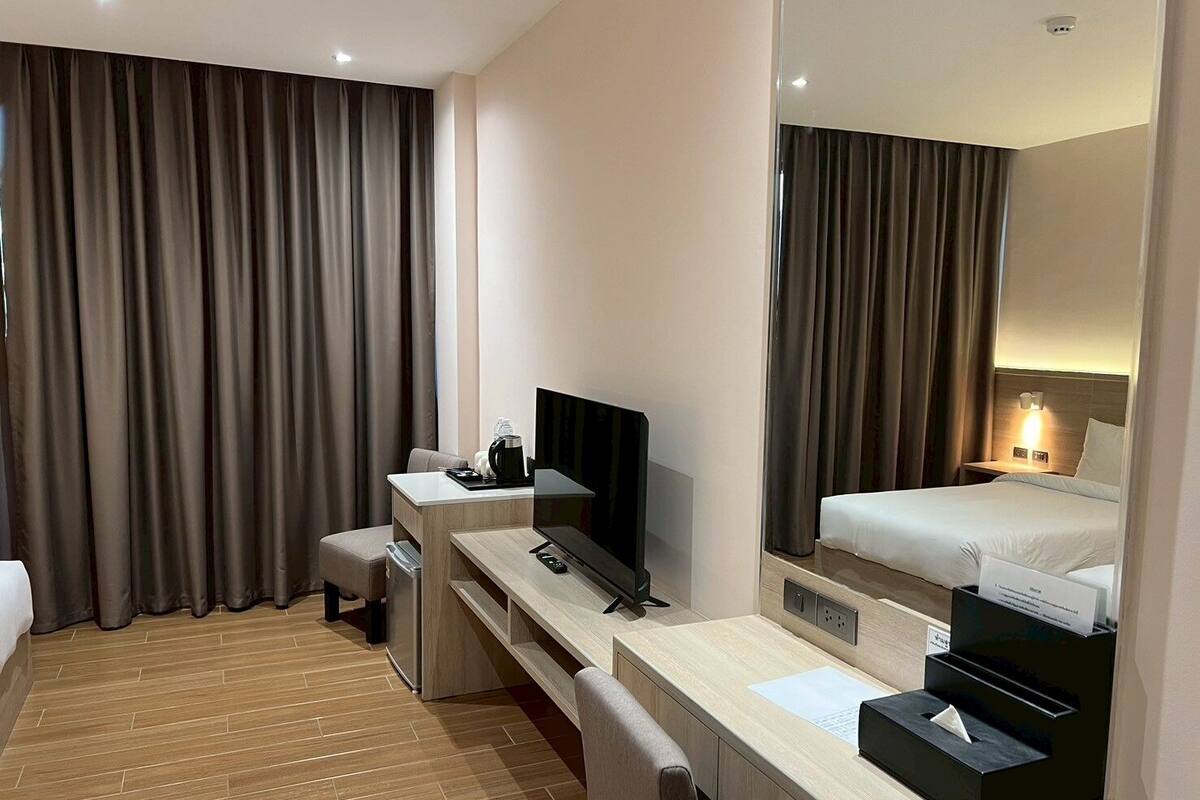 Quarto de hotel moderno com uma cama grande, uma escrivaninha com computador, televisão e máquina de café.