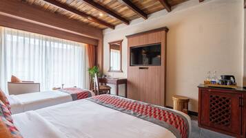 Quarto de hotel com duas camas, teto de madeira, televisão, escrivaninha e armário.