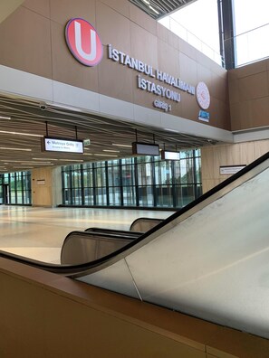 Área interna com sinalização do Aeroporto de Istambul, um corrimão rolante e indicação de acesso ao metrô.