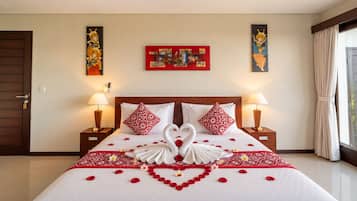 Quarto de hotel com uma cama grande, duas mesas de cabeceira, uma porta de madeira e obras de arte nas paredes.