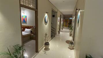 Corredor de hotel com cama, plantas em vasos e quadros nas paredes.