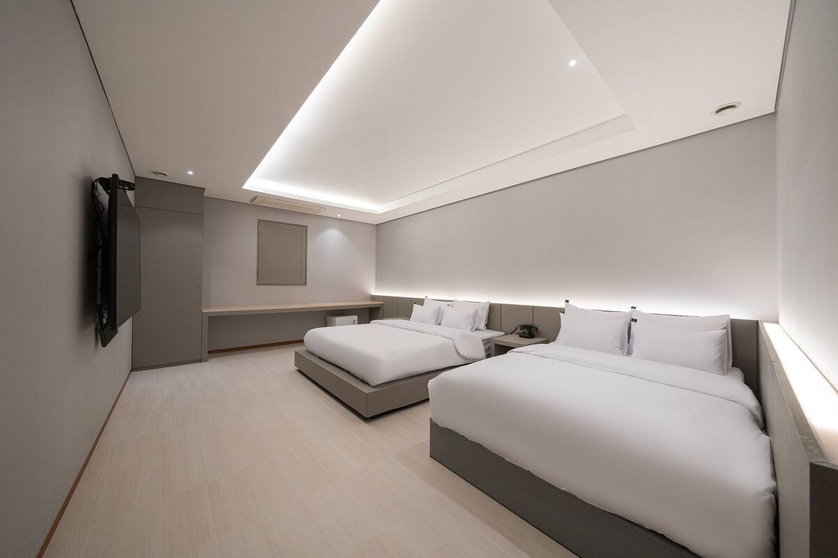 Quarto de hotel moderno com duas camas, uma televisão de tela plana na parede e um claraboia.