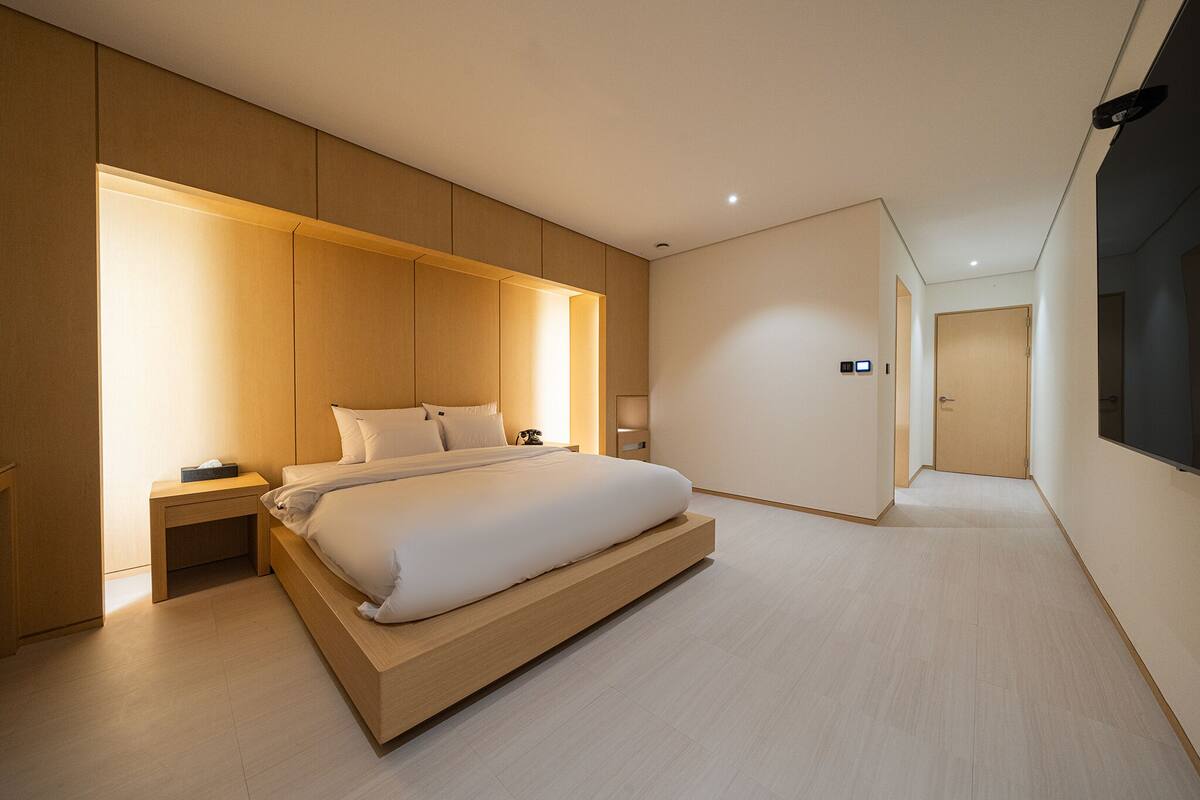 Quarto moderno com uma cama grande, cabeceira de madeira, mesas de cabeceira e uma TV de tela plana na parede.