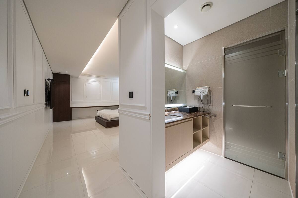Quarto de hotel moderno com uma cama grande, banheiro com chuveiro de vidro e closet espaçoso.