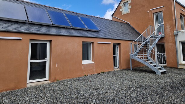 Um edifício com telhado inclinado, painéis solares, escadas e chão de cascalho.