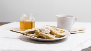 Um prato com fatias de pão e uma porção de manteiga, um pote de mel e uma xícara branca sobre um tecido branco.