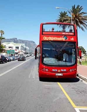 Um ônibus de dois andares vermelho com a inscrição 'CitySightseeing' em uma rua da cidade, com palmeiras e edifícios ao fundo.