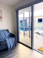 Uma sala de estar moderna com um sofá cinzento e uma grande porta de vidro deslizante que dá para um deck de madeira com piscina.