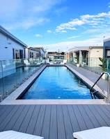 Uma piscina retangular com grades de vidro em ambos os lados, rodeada por um deck de madeira.