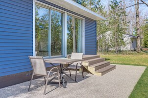 Um pátio com mesa e cadeiras, um deck de madeira e uma casa com revestimento azul e janelas grandes.
