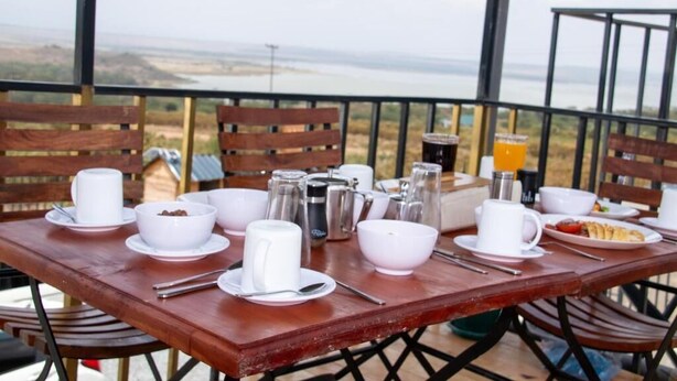 Mesa de café da manhã posta com pratos, xícaras e cafeteira, com vista panorâmica.