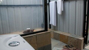 Casa de banho com uma pia branca, uma janela com vista, um porta-toalhas e um par de chinelos sobre um tapete.