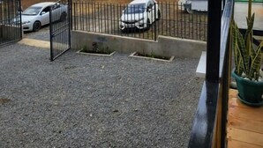 Vista de varanda com vista para um estacionamento, onde se vê um carro branco e uma van branca, céu nublado e paisagem distante.