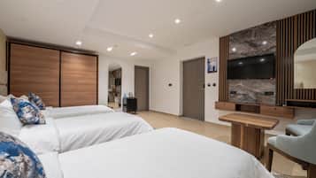Quarto de hotel moderno com duas camas, um guarda-roupa de madeira, uma televisão fixada numa parede de mármore e uma pequena mesa de madeira.