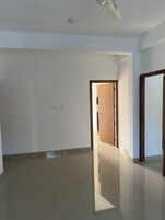 Um quarto amplo e vazio, com piso de azulejos brilhantes, paredes brancas e uma porta de madeira.
