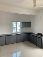 Uma cozinha moderna com bancada preta, armários brancos e uma janela com vista para edifícios.