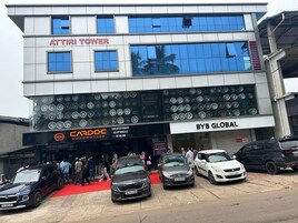 Um edifício com vários estabelecimentos, incluindo 'ATTIRI TOWER', 'CARDOC AUTOMOTIVE' e 'BYB GLOBAL'. Vários carros estão estacionados na frente.