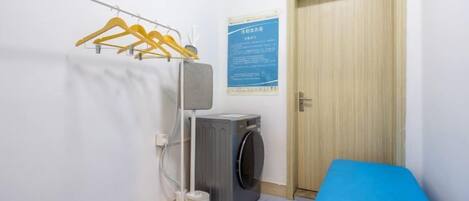 Quarto pequeno com colchão azul, máquina de lavar e porta de madeira.