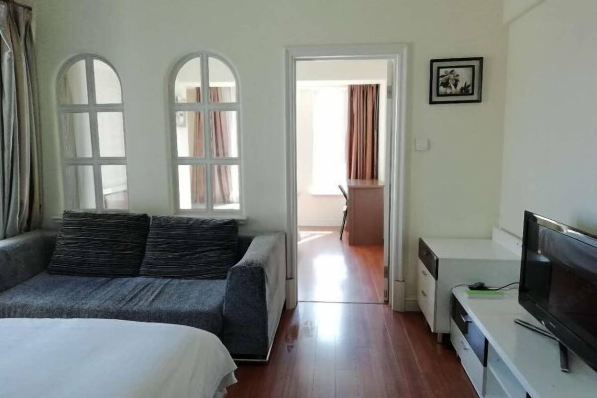 Um quarto com cama, sofá, televisão e porta que dá para outro cômodo.