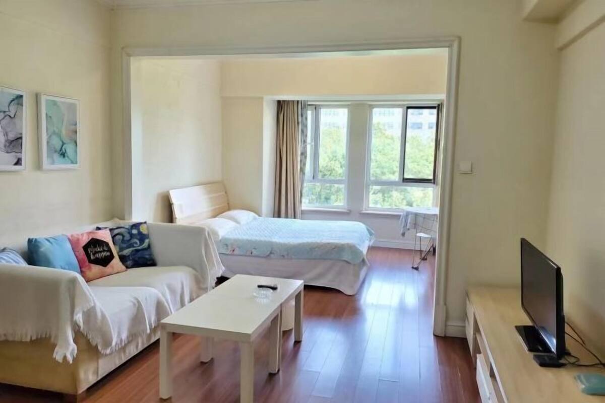 Quarto com cama, sofá, televisão e janela.