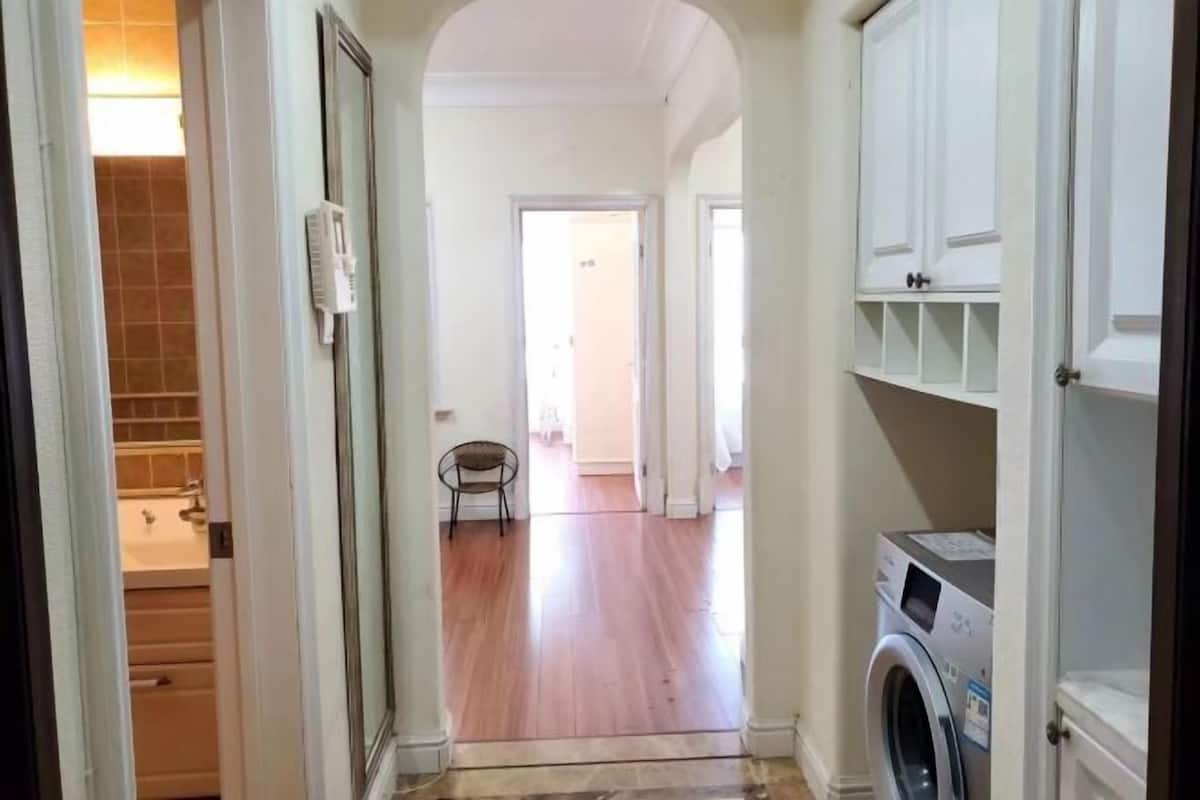 Corredor com máquina de lavar, uma cadeira e porta que dá para outro quarto.