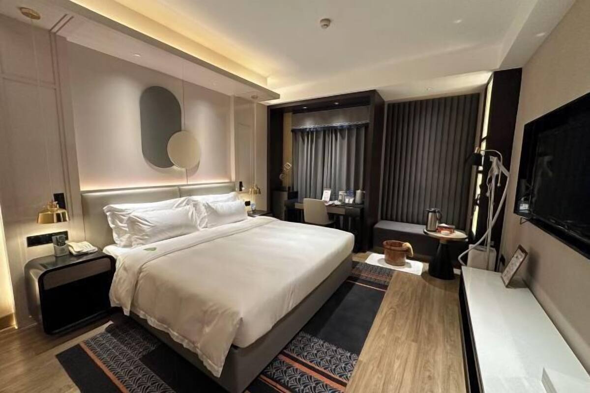 Quarto de hotel moderno com uma cama grande, mesas de cabeceira, escrivaninha, televisão e uma janela com cortinas.