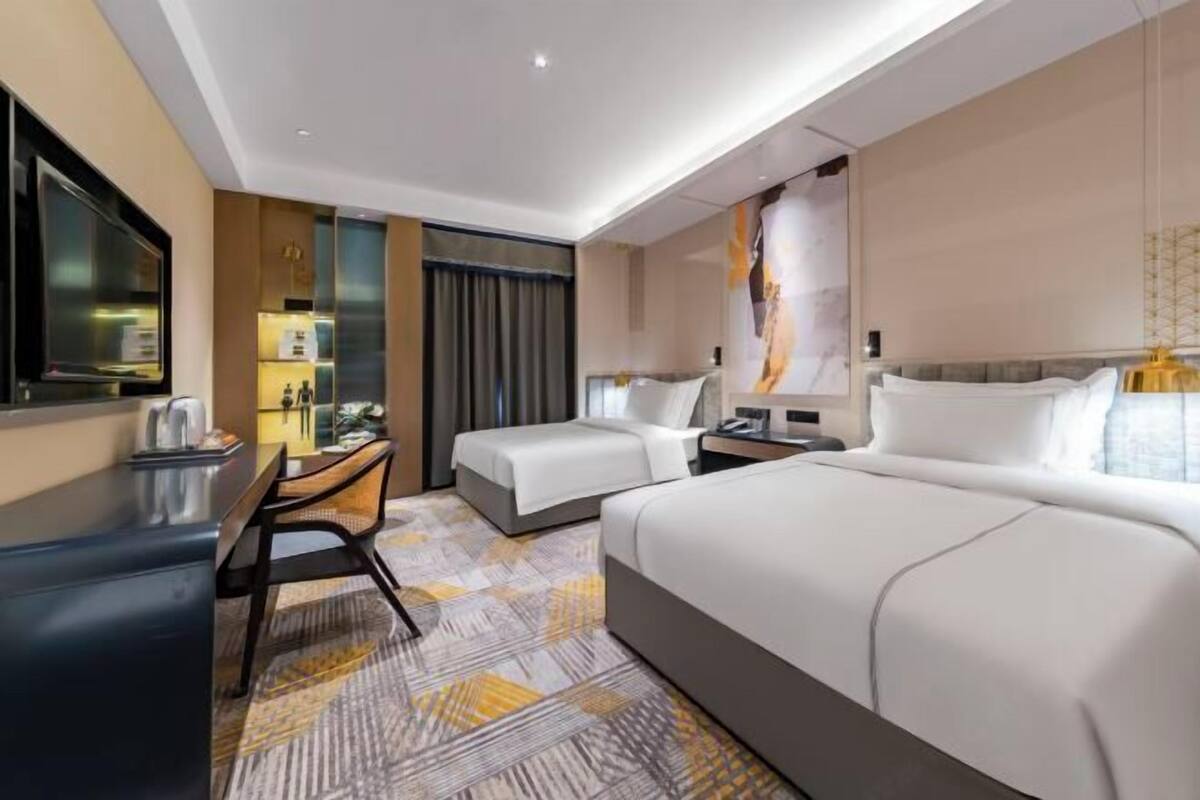 Quarto de hotel com uma cama grande, uma cama menor, uma escrivaninha com cadeira e uma televisão.
