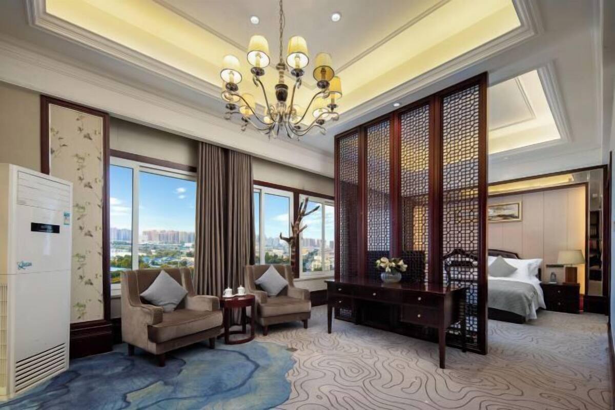 Quarto de hotel com uma grande janela, um candelabro, um sofá, uma escrivaninha e uma cama.