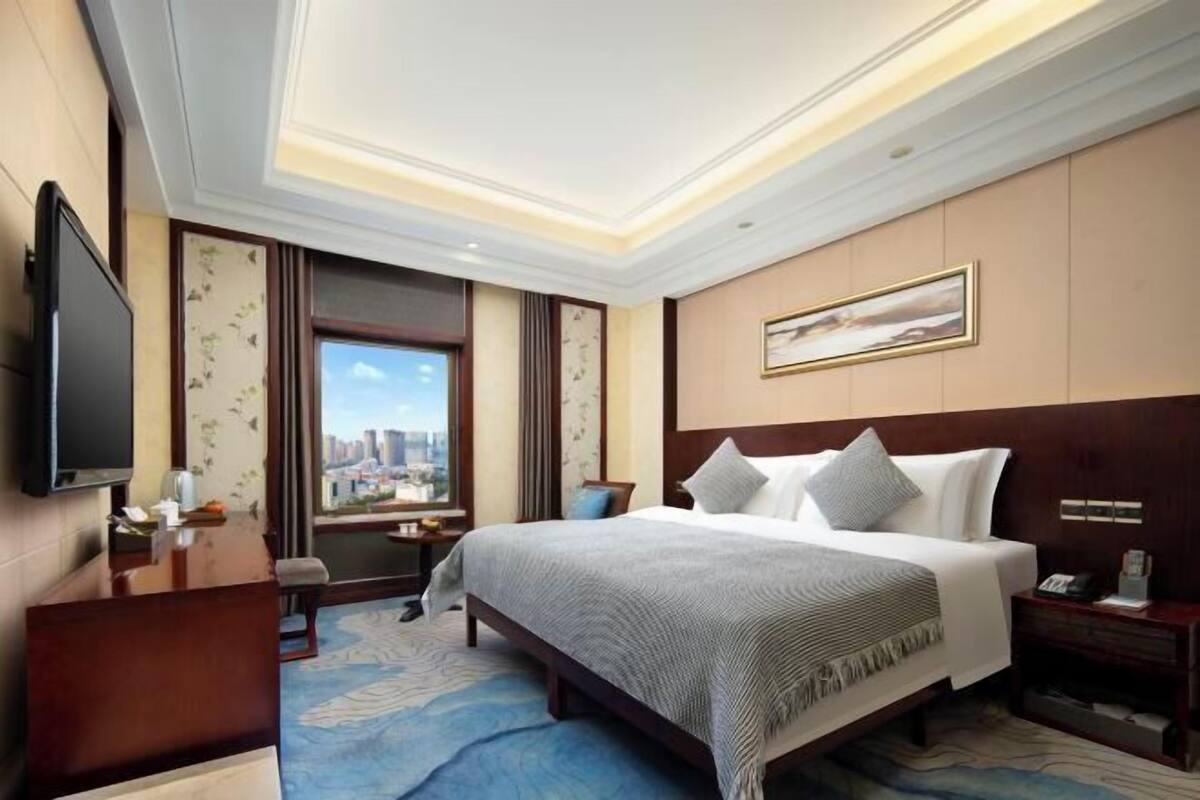 Quarto de hotel com uma cama grande, uma escrivaninha, uma televisão e vista para a cidade.