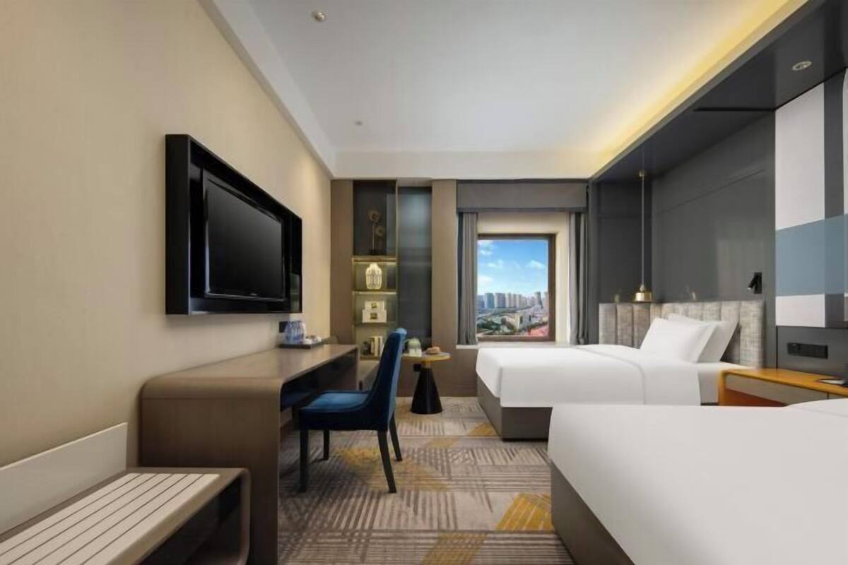Quarto de hotel com cama, escrivaninha, cadeira, televisão e vista para a cidade.