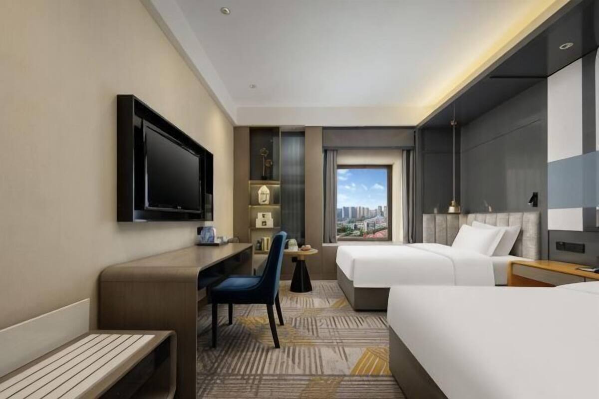 Quarto de hotel com cama, escrivaninha, cadeira, televisão e vista para a paisagem urbana.