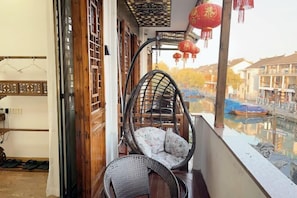 Quarto tradicional com porta de madeira, uma cadeira de vime e vista para um canal com barcos.