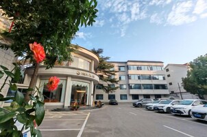 Um hotel com entrada curva, vários andares e estacionamento com diversos carros.