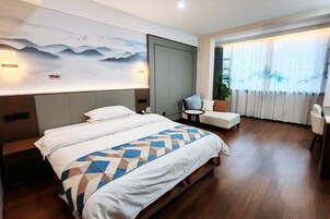 Quarto de hotel com uma cama grande, uma escrivaninha, uma cadeira e vista para o exterior através de uma janela.