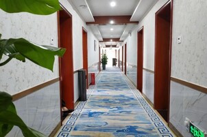 Corredor de hotel com carpete estampado, portas vermelhas e uma lixeira.